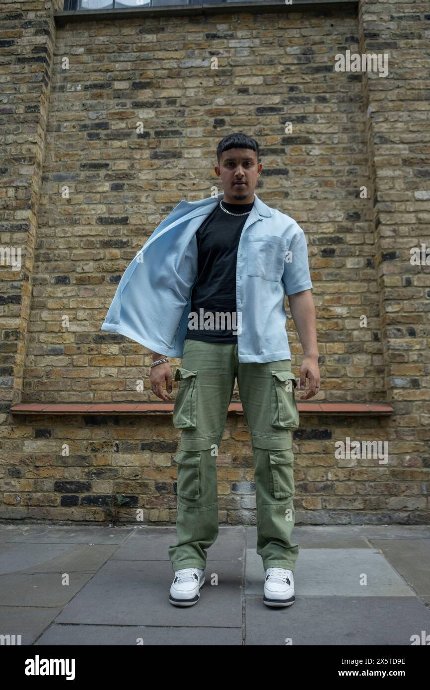 Man wearing unbuttoned shirt and cargo pants standing in front of brick ...