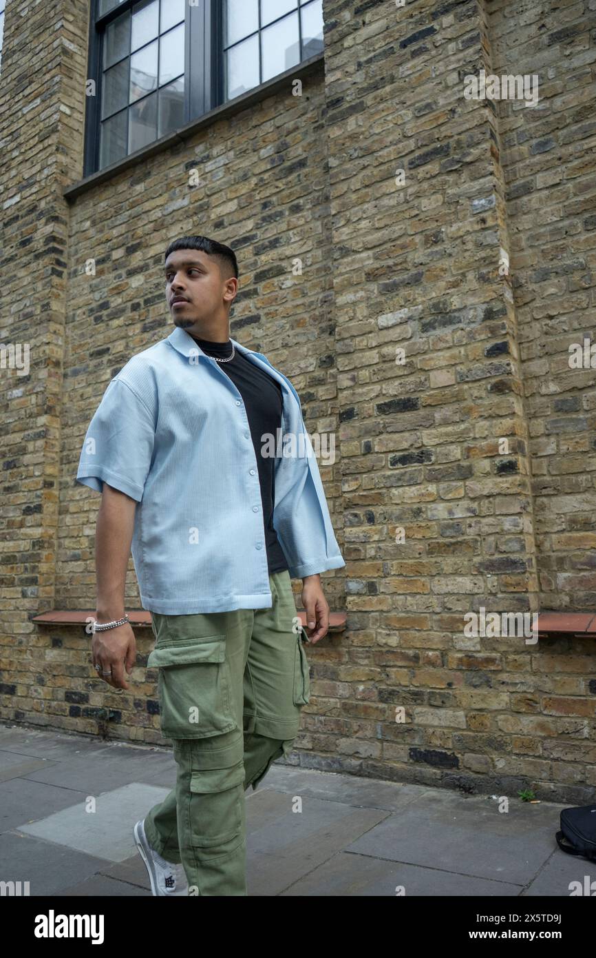 Man wearing unbuttoned shirt and cargo pants walking along brick wall ...