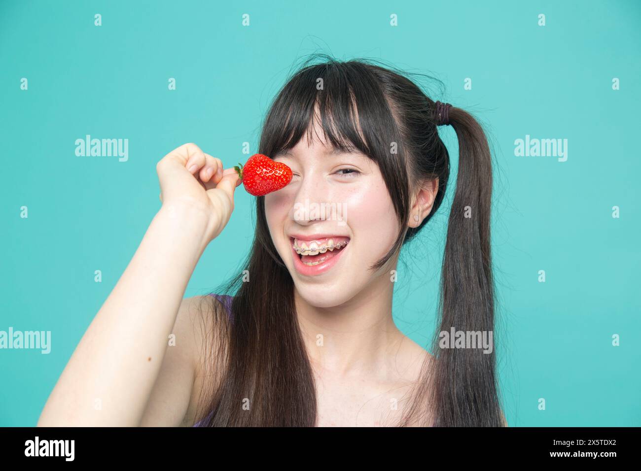 Studio portrait of smiling girl holding strawberry in front of eye ...