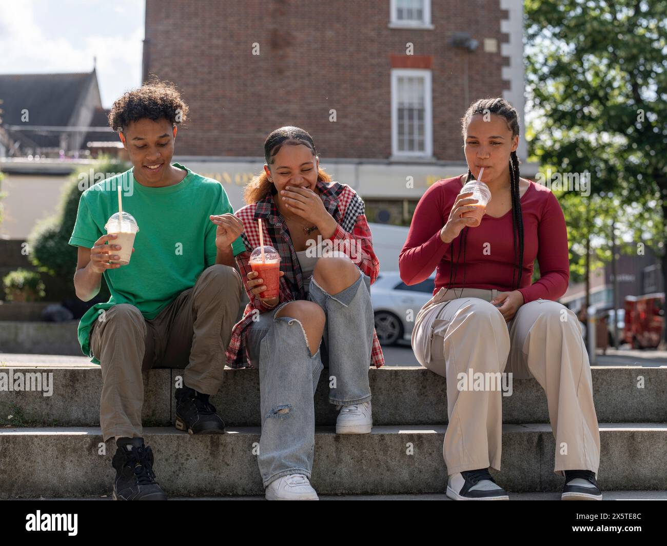 Friends laughing while drinking smoothies on steps Stock Photo - Alamy