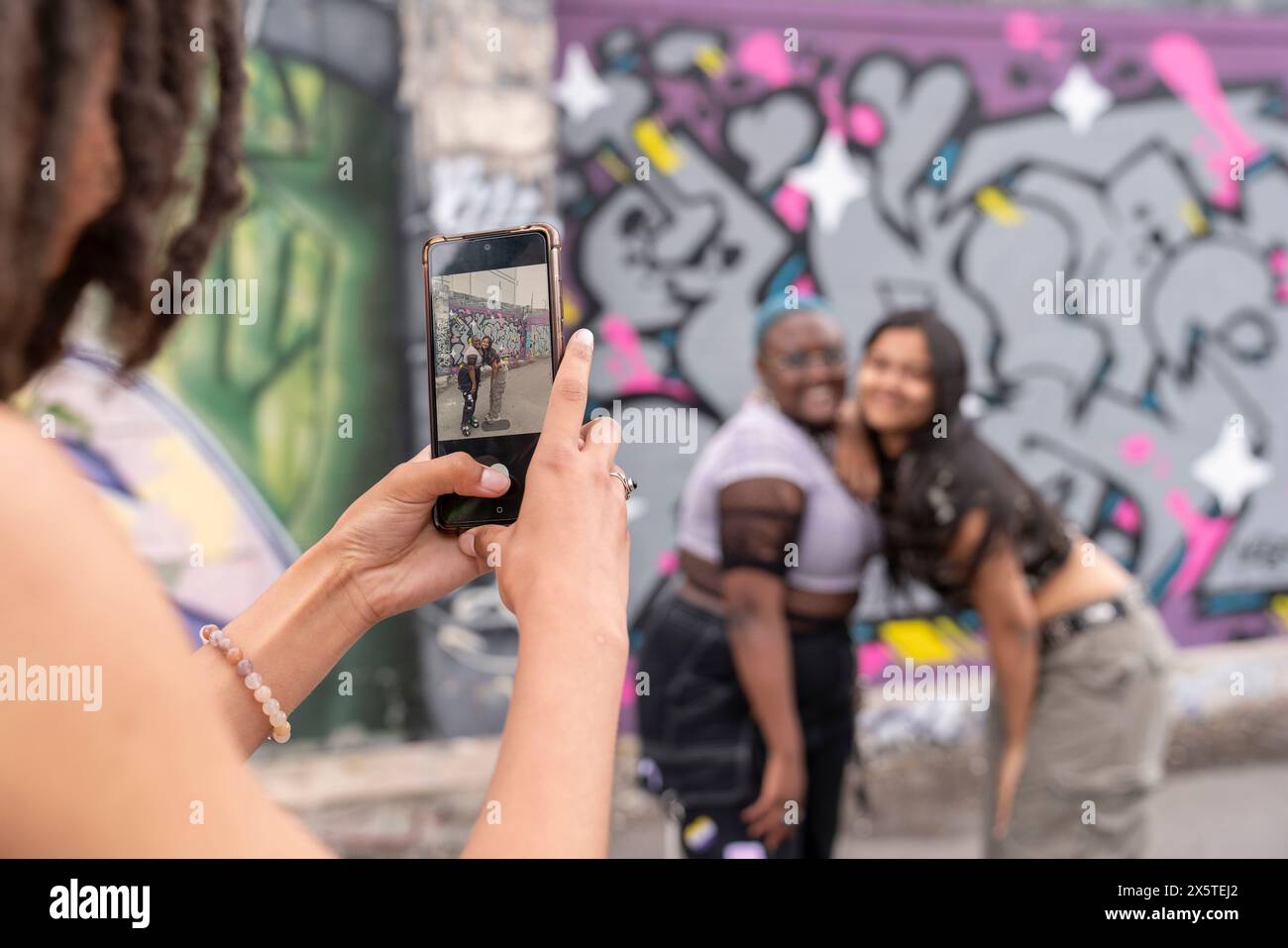 Woman photographing friends against graffiti wall Stock Photo - Alamy