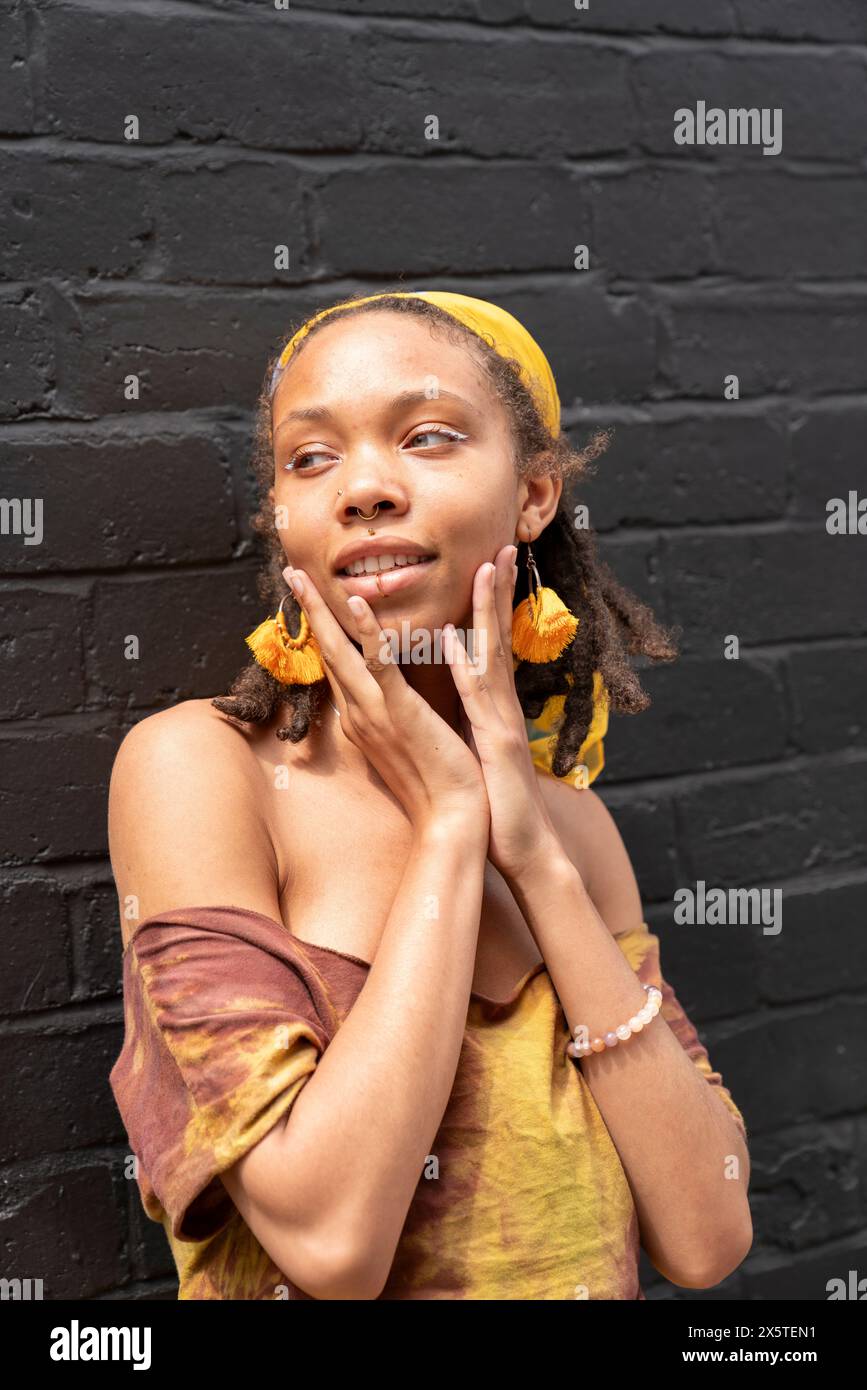 Portrait of young woman standing against brick wall Stock Photo - Alamy