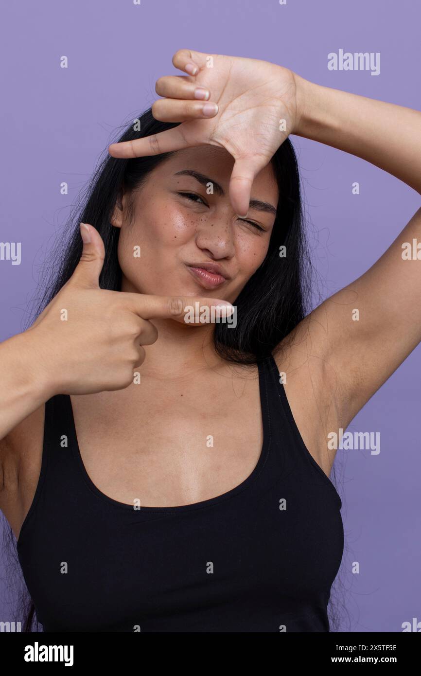 Woman with black hair forming frame with hands and looking at camera ...