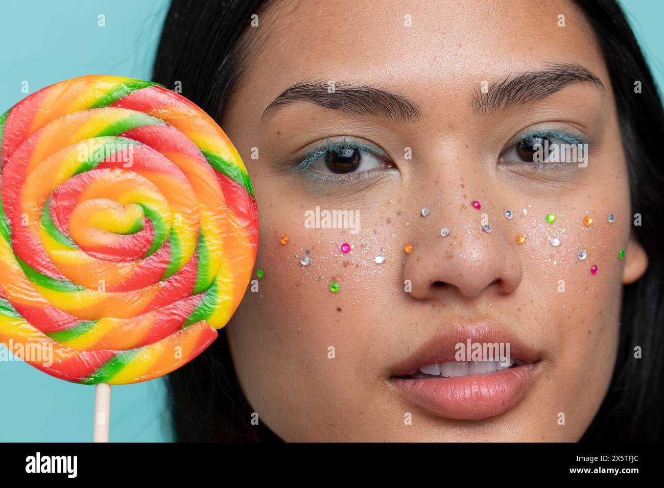 Portrait of woman wearing shiny freckles, holding colorful lollipop ...