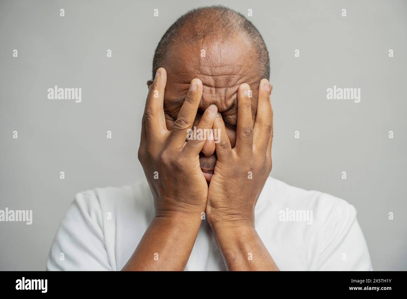 Portrait of man covering head with hands against gray background Stock ...