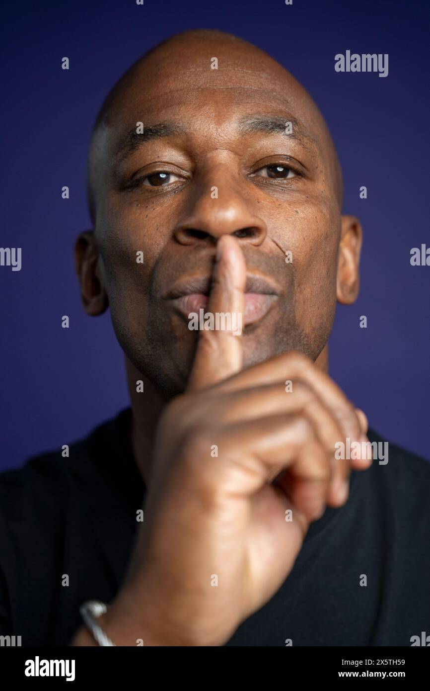 Portrait of man with finger on lips against purple background Stock ...