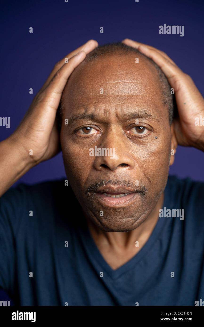 Portrait of worried man with hands on head against purple background ...