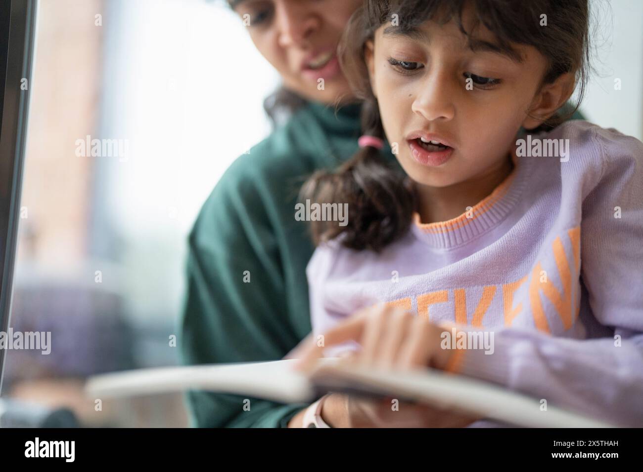 Mother and daughter reading book near window Stock Photo - Alamy
