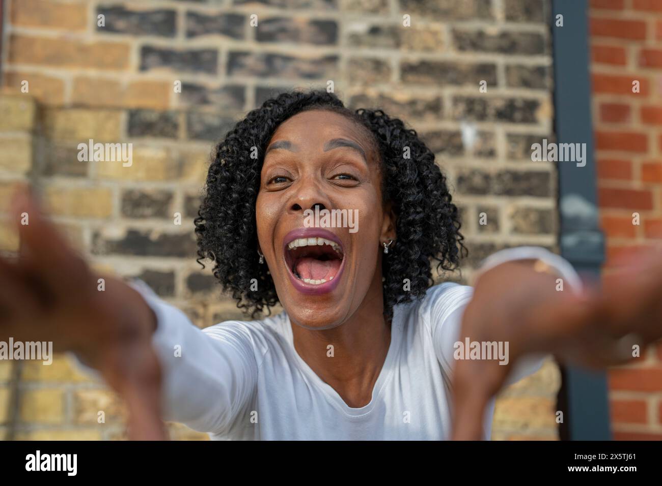 Portrait of woman reaching hands against brick wall Stock Photo - Alamy