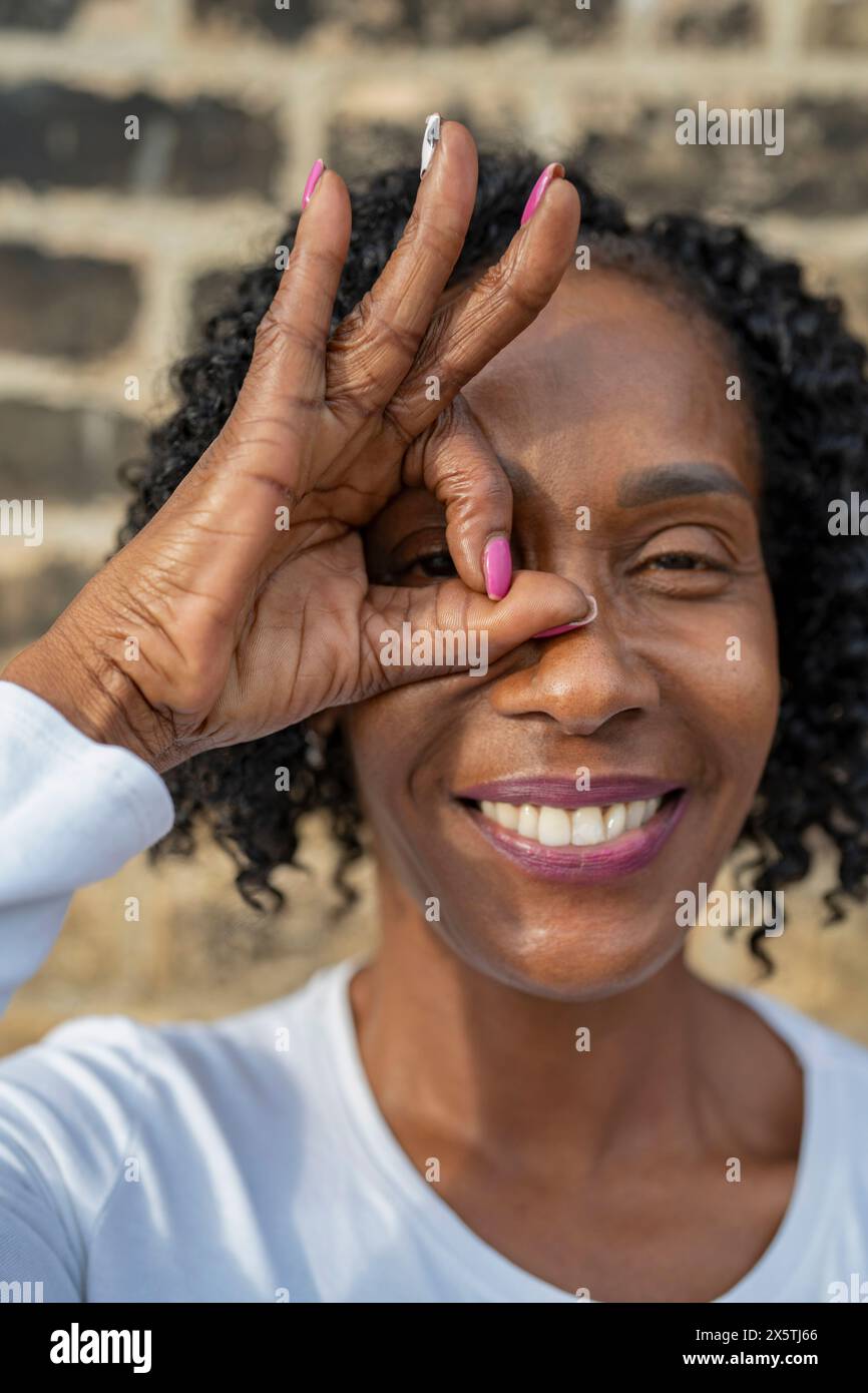 Portrait of woman looking through OK sign made with fingers against ...