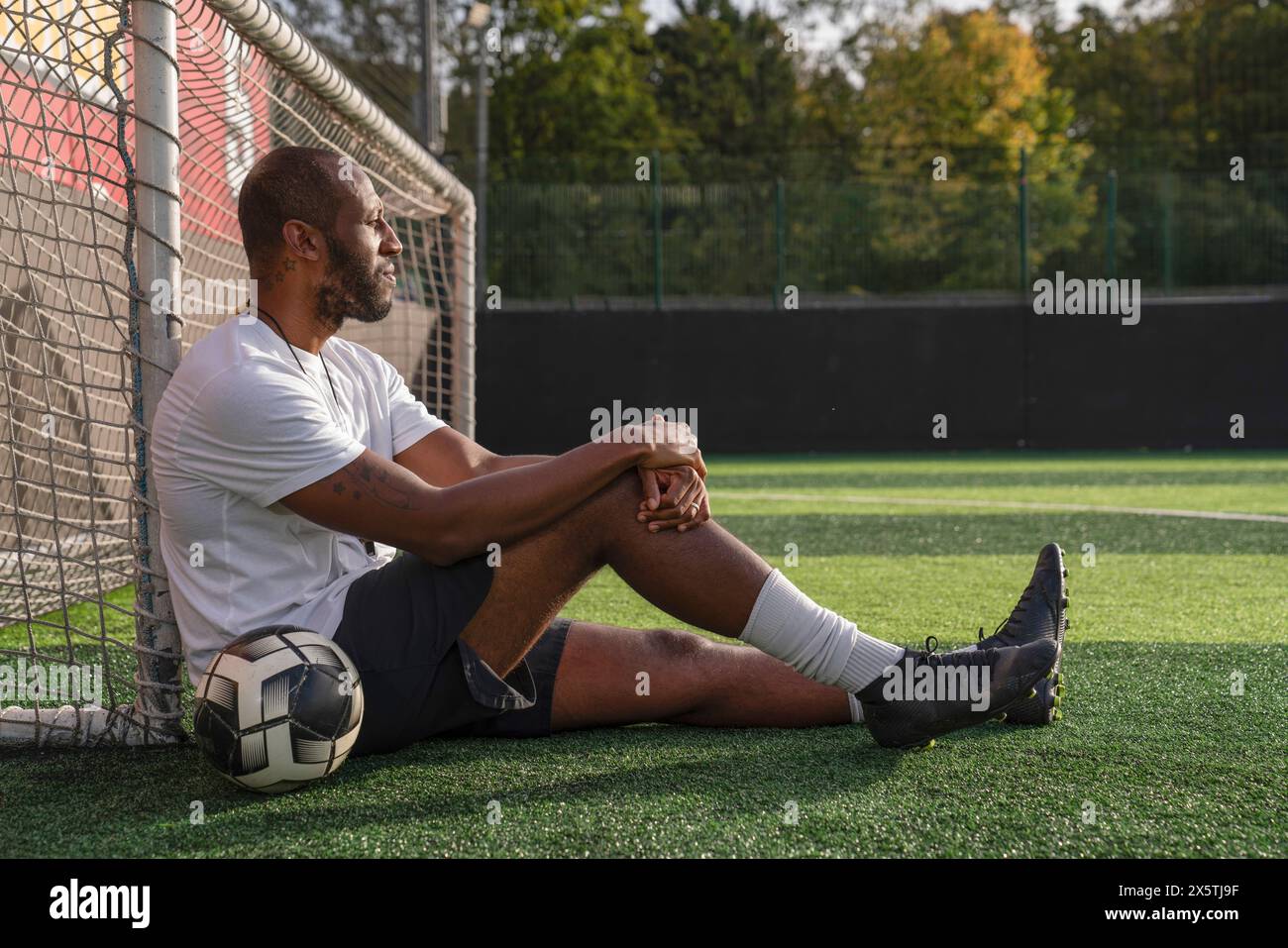 Man with ball sitting next to soccer goal Stock Photo - Alamy