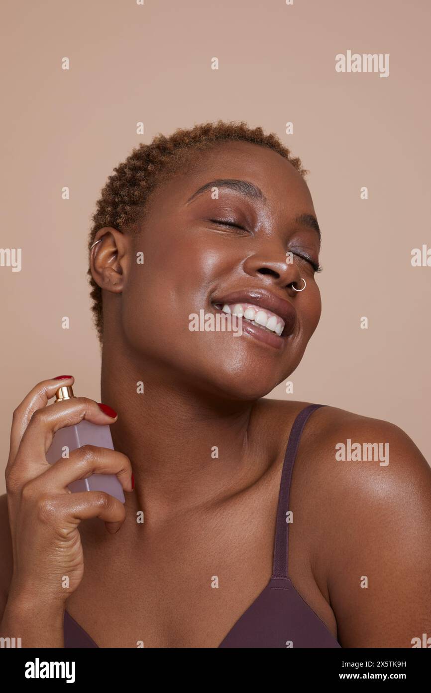 Studio portrait of smiling woman spraying perfume on neck Stock Photo ...