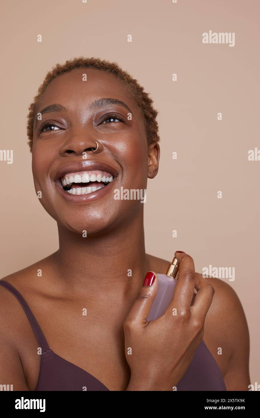 Studio portrait of smiling woman spraying perfume on neck Stock Photo ...