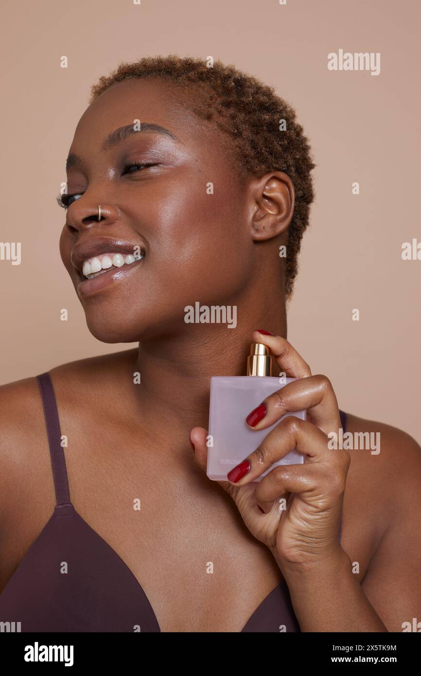 Studio portrait of smiling woman spraying perfume on neck Stock Photo ...