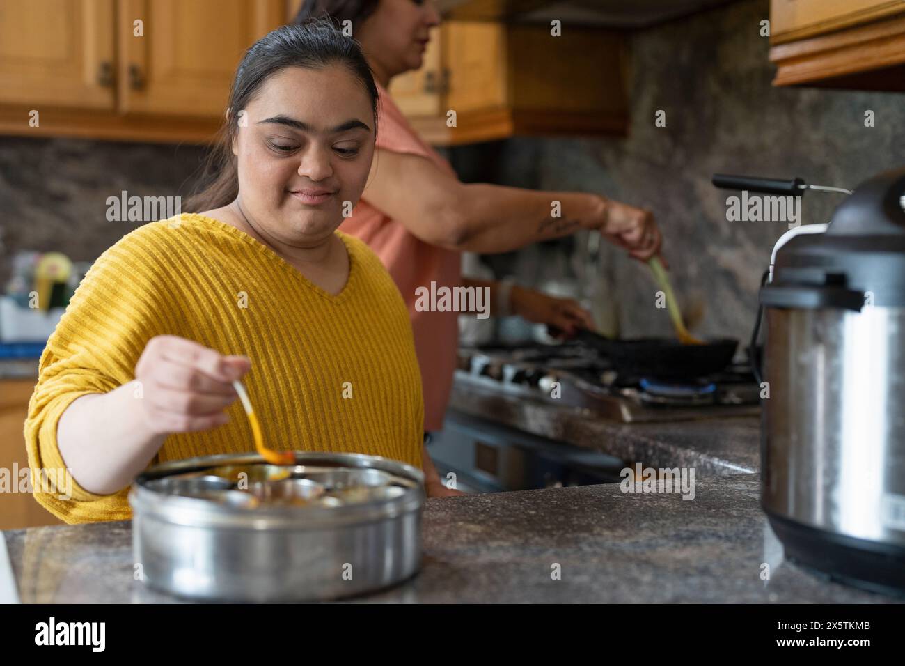 Woman with down syndrome adding spices while cooking with mother in ...