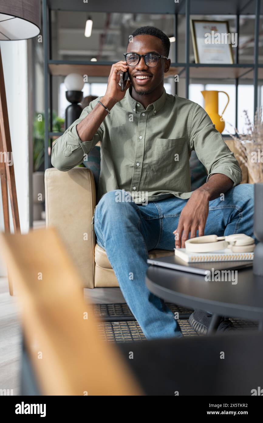 Young man with smartphone sitting in office lounge Stock Photo - Alamy