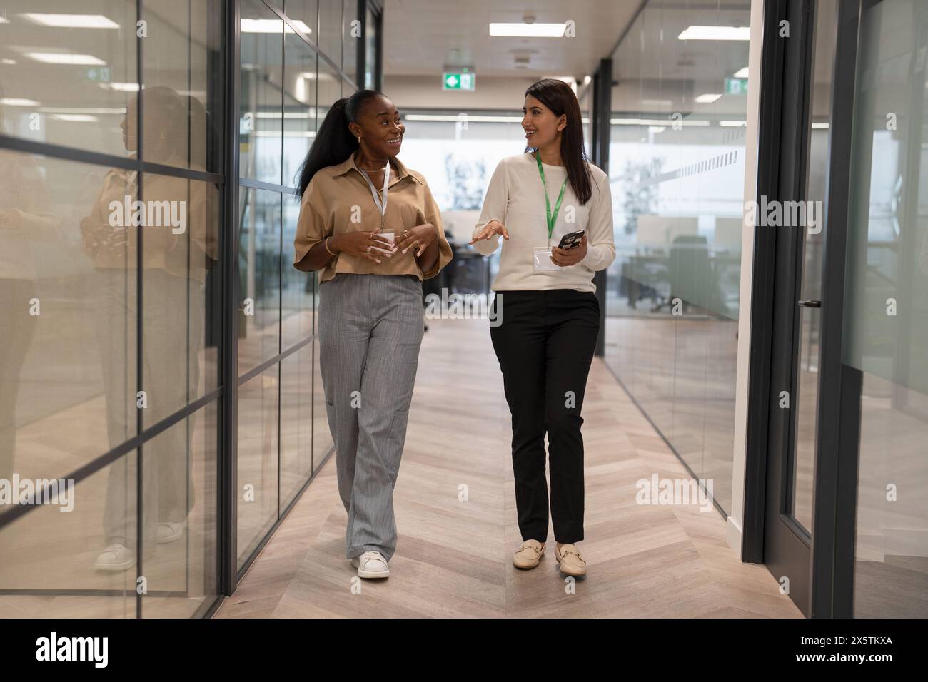 Two businesswomen walking together in office corridor Stock Photo - Alamy