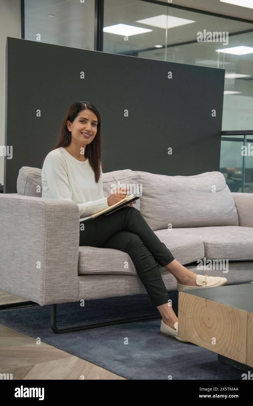 Portrait of woman sitting on sofa and writing in notepad Stock Photo ...