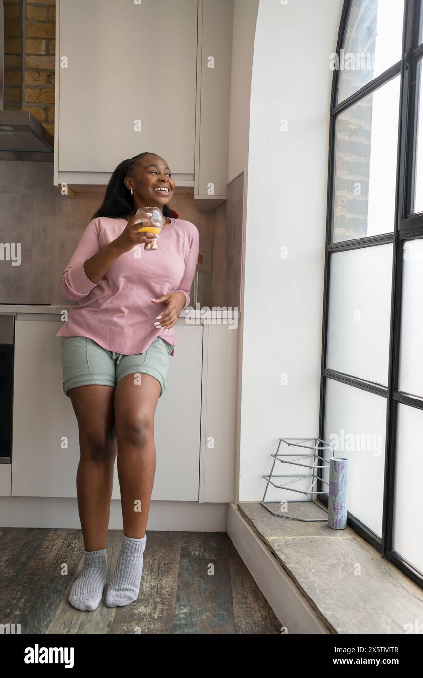 Smiling woman standing and looking through kitchen window Stock Photo ...