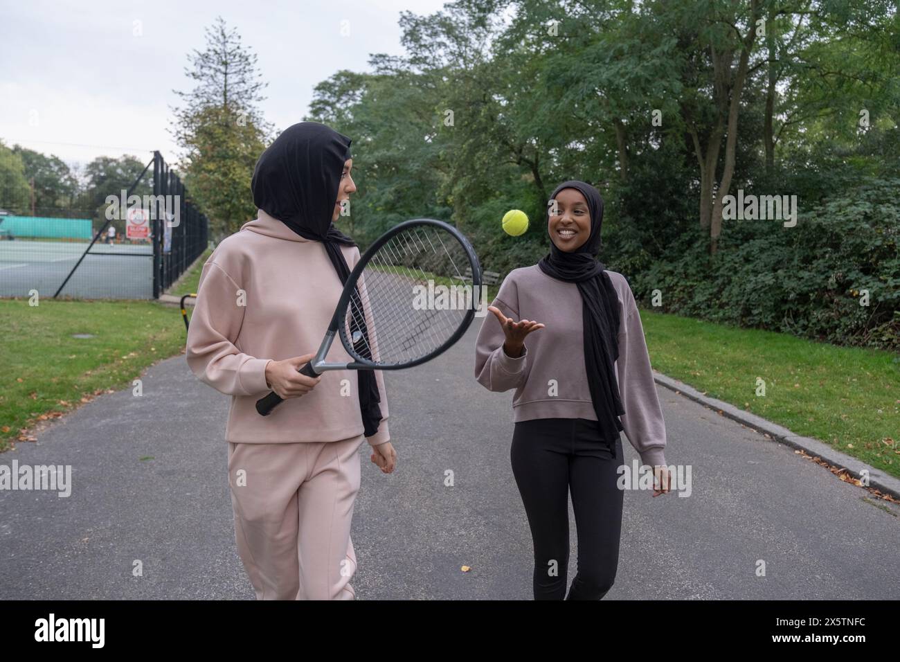 Two women in hijabs walking in park with tennis racket and ball Stock ...
