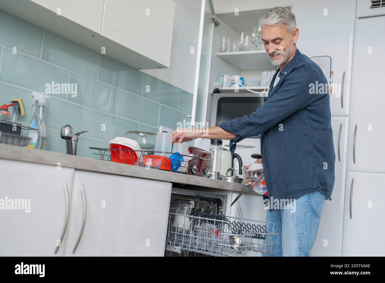 Smiling mature man loading dishwasher at home Stock Photo - Alamy