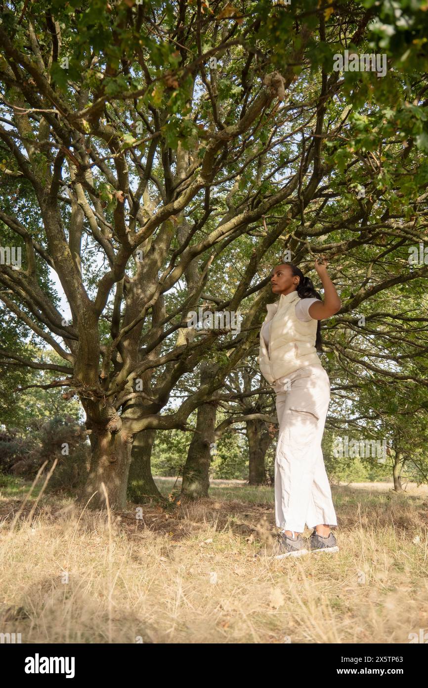 Young woman standing under tree in grassy field Stock Photo - Alamy