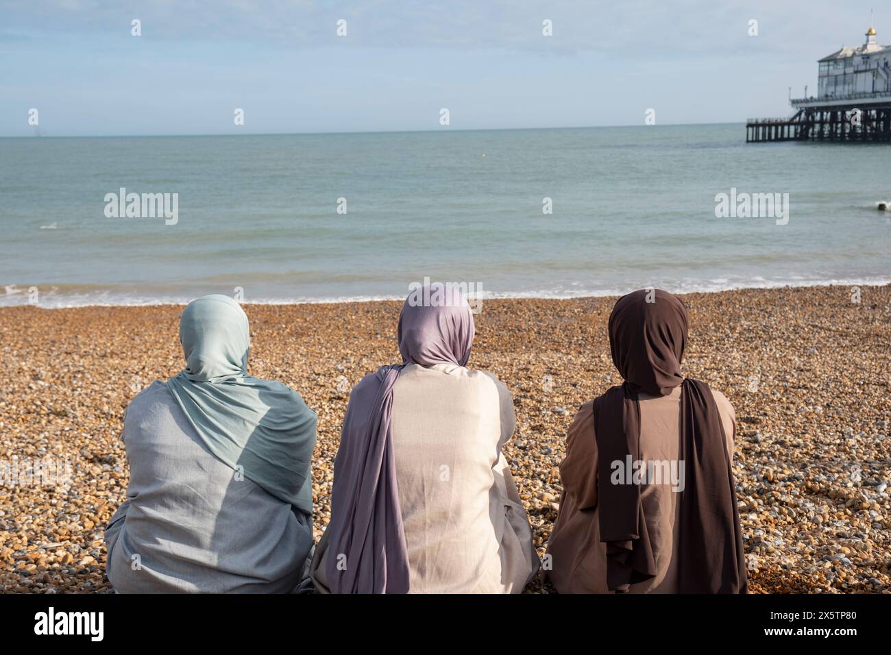Three Muslim women looking at sea while sitting on beach Stock Photo ...