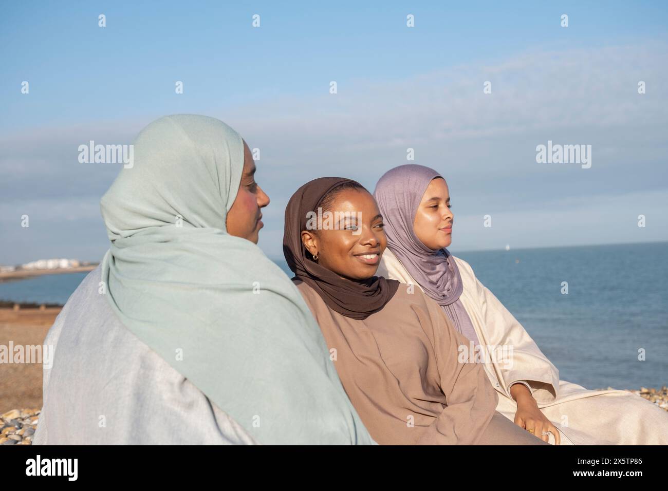 Three Muslim friends sitting on beach Stock Photo - Alamy