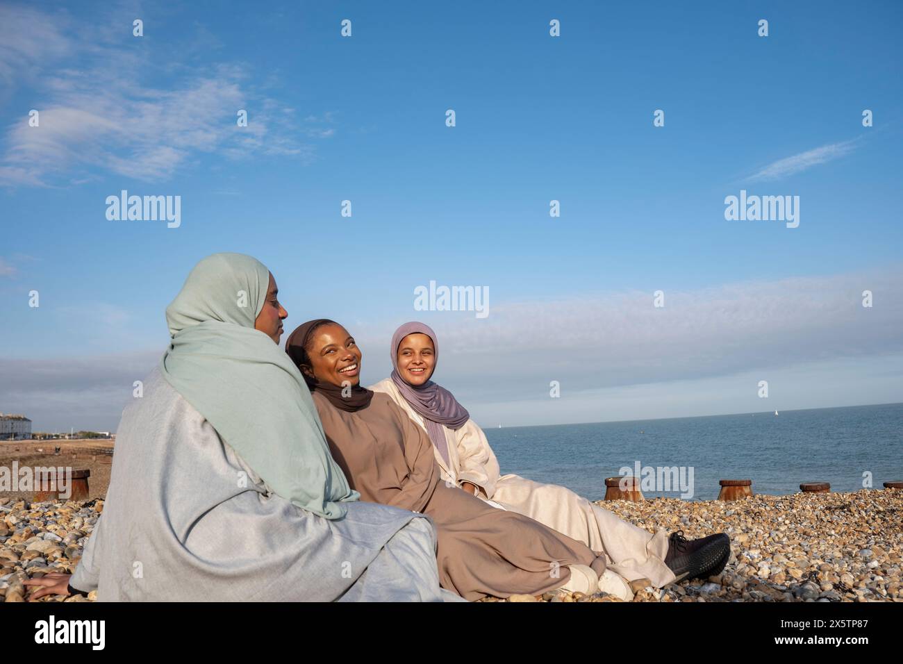 Three Muslim friends laughing while sitting on beach Stock Photo - Alamy