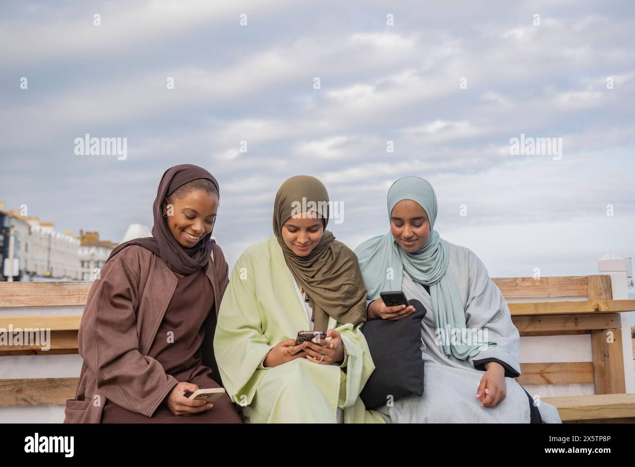 Three Muslin women using smart phones while sitting on bench Stock ...