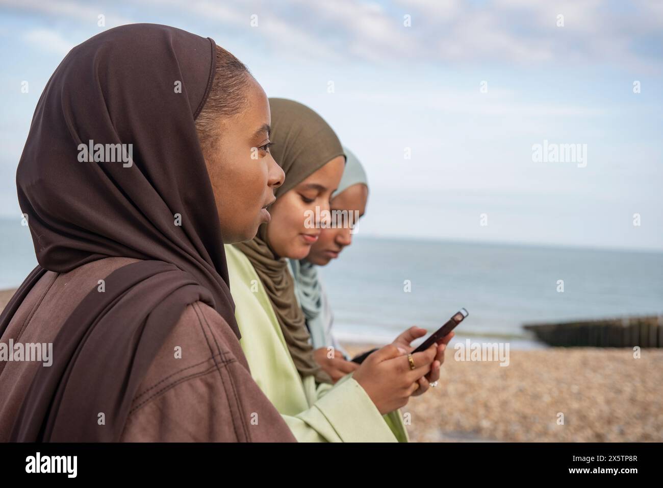 Three Muslin women using smart phones on beach Stock Photo - Alamy