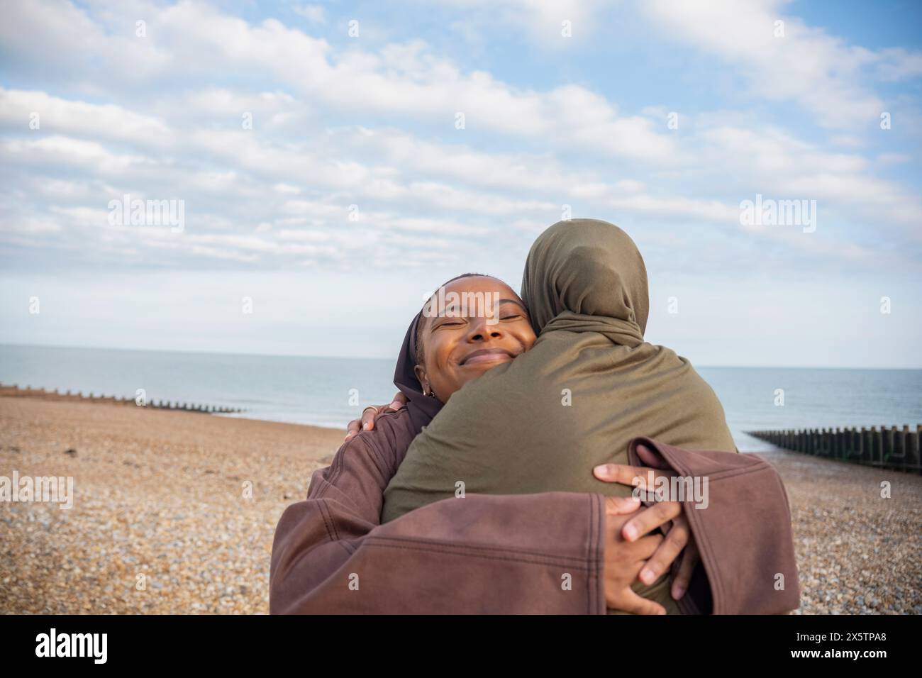 Two Muslim women embracing on beach Stock Photo - Alamy