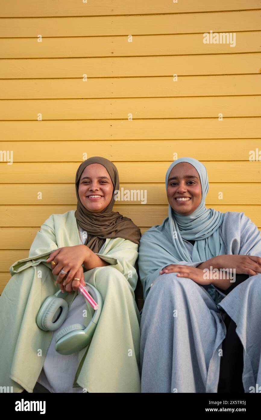 Portrait of Muslim friends sitting by yellow wall Stock Photo - Alamy