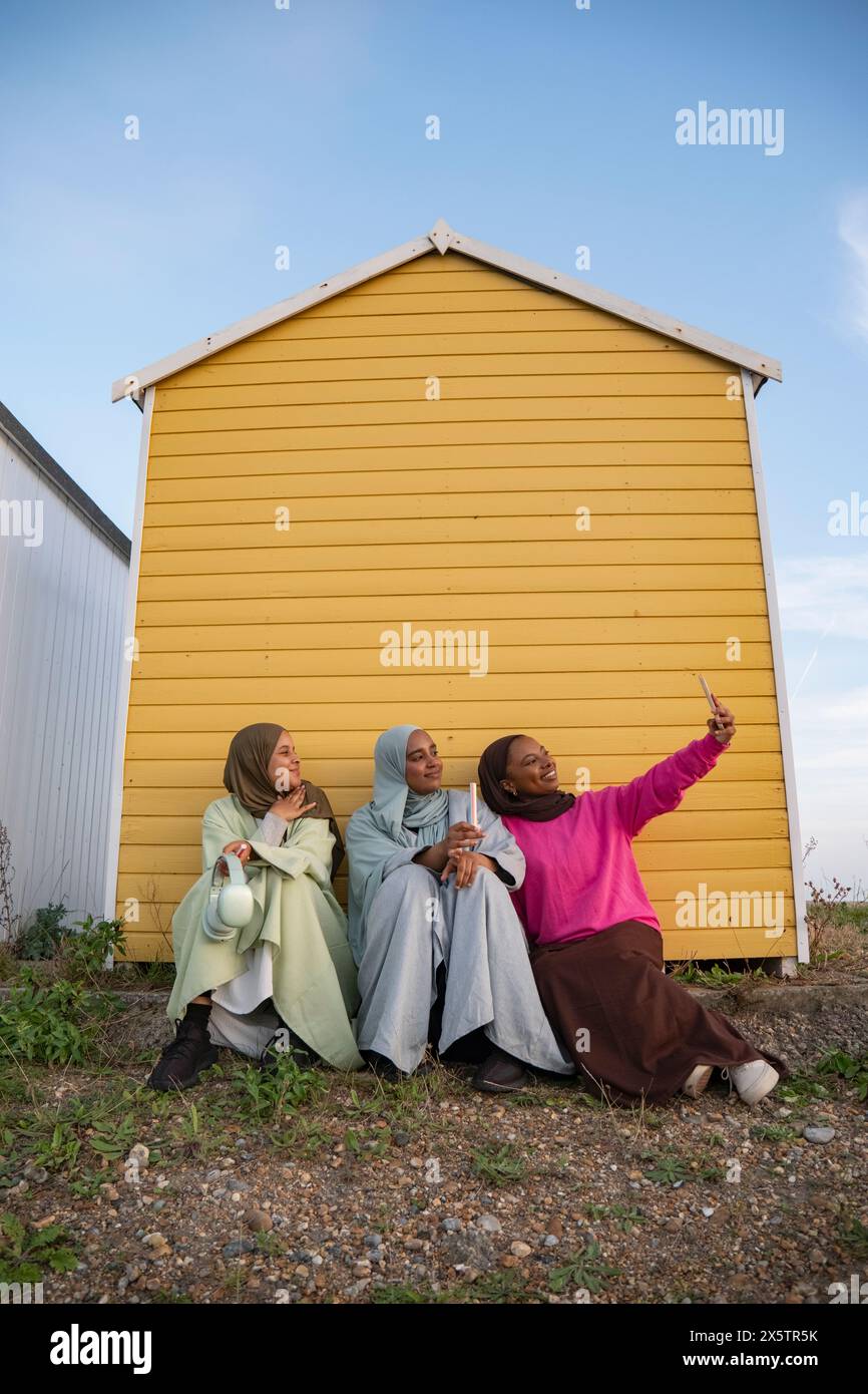 Three Muslim friends taking selfie while sitting by beach hut Stock ...