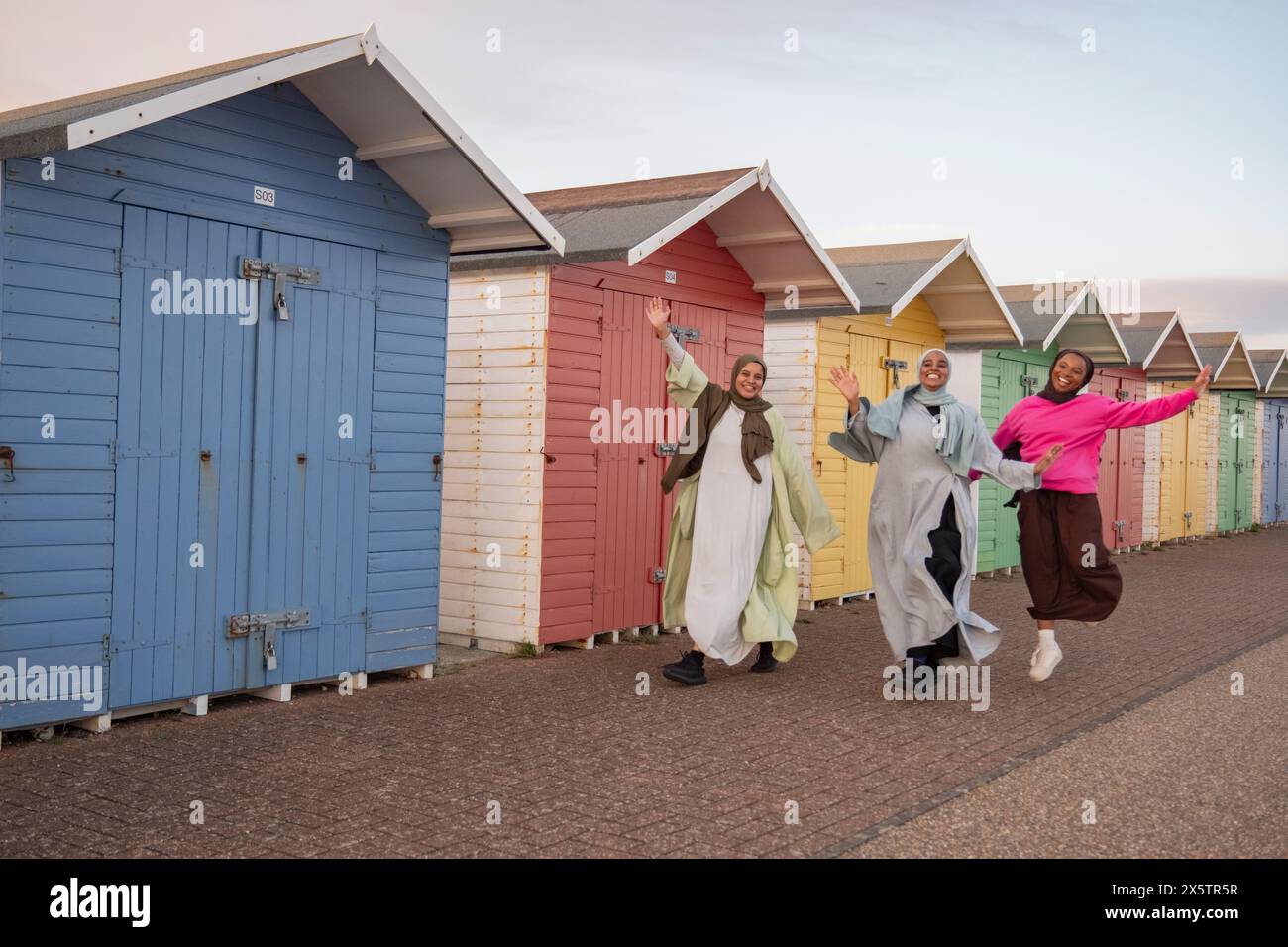 Cheerful Muslim friends waving while walking next to beach huts Stock ...