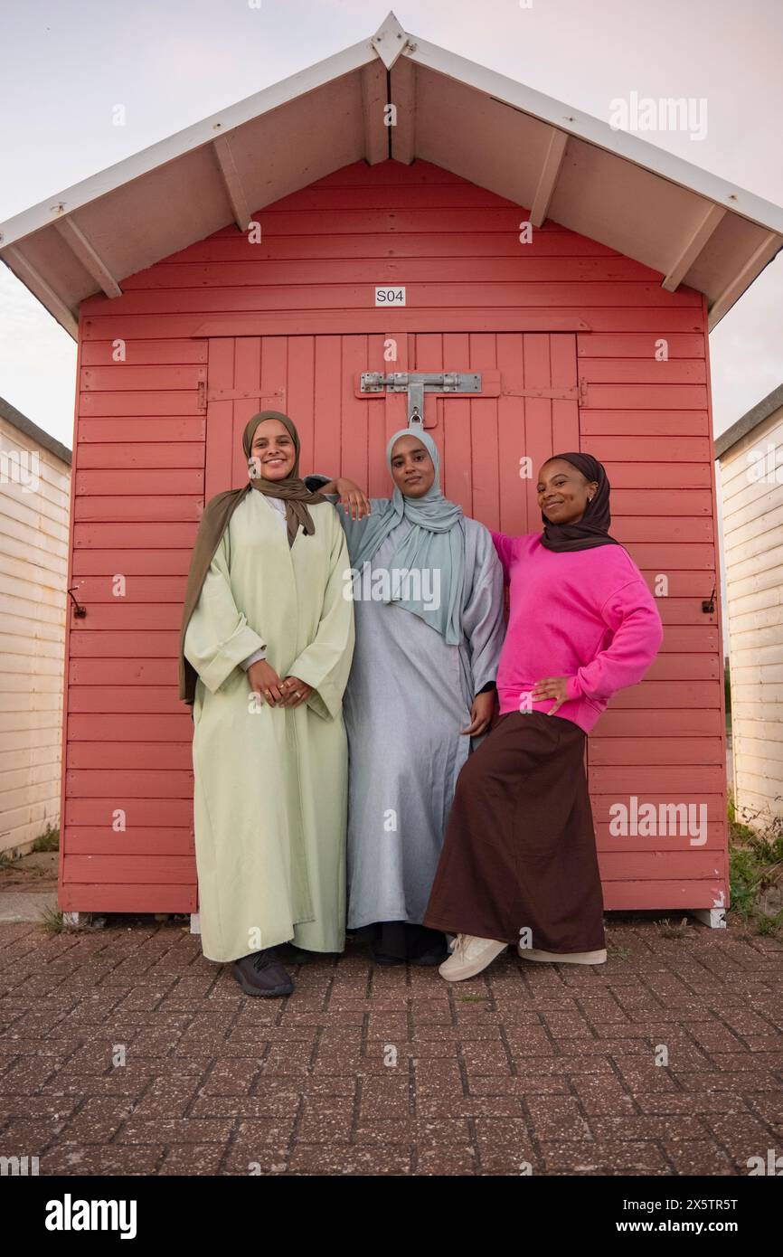 Portrait of three Muslim friends standing in front of red beach hut ...