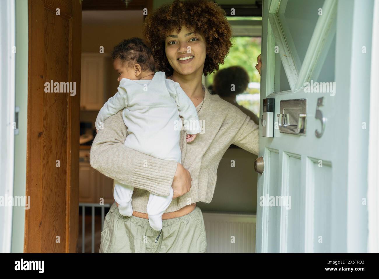 Smiling mother holding baby daughter at home entrance Stock Photo - Alamy