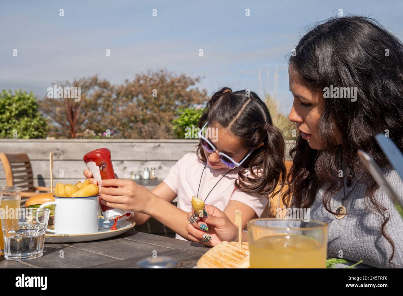 Mother and daughter eating burgers and french fries in outdoor ...