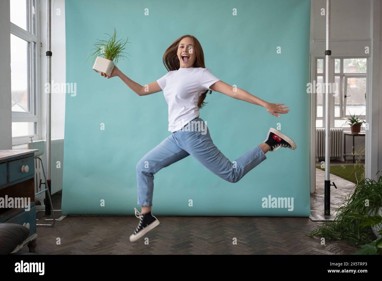 Studio portrait of teenage girl jumping with small potted plant in hand ...