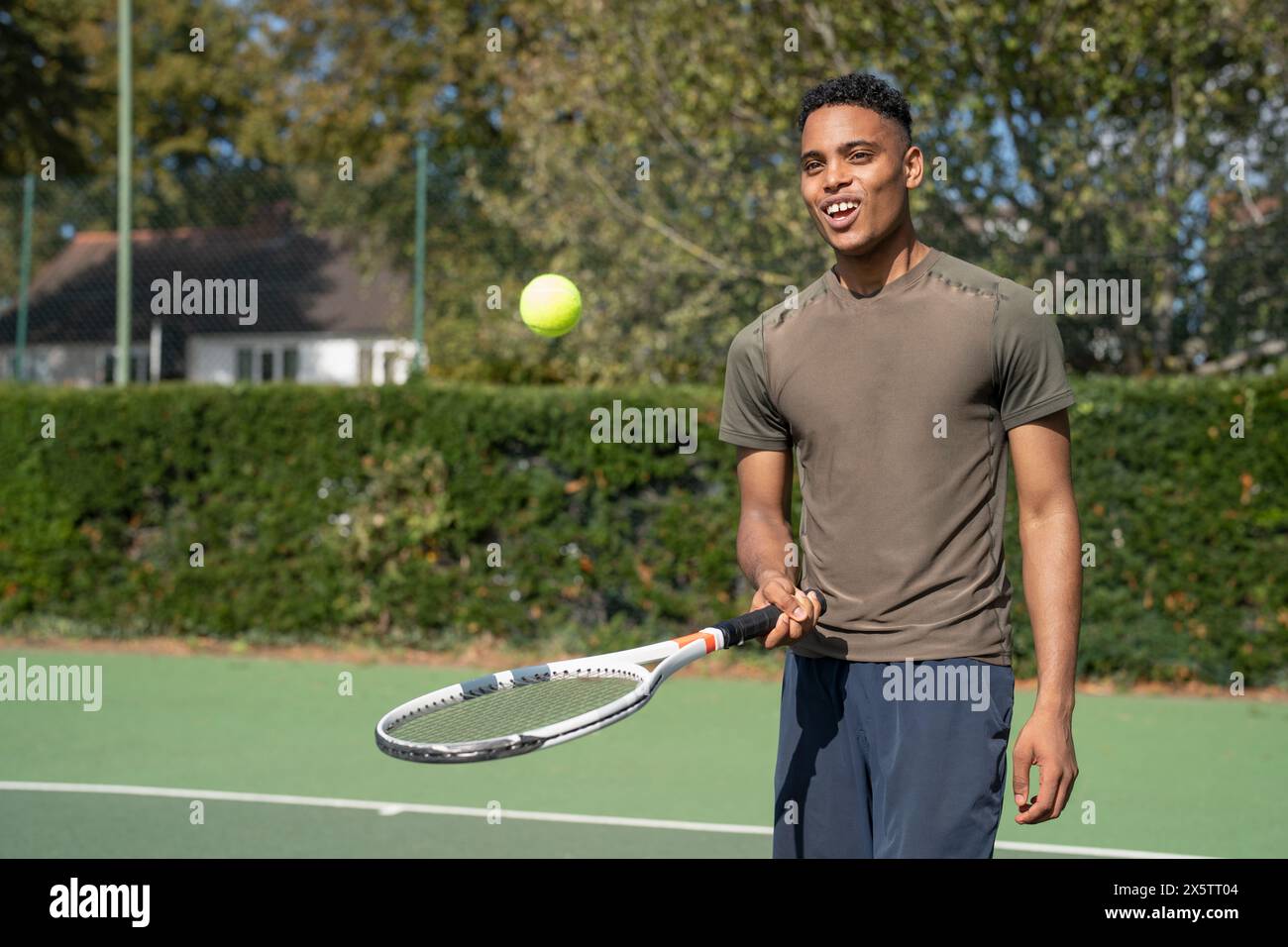 Smiling man bouncing tennis ball in tennis court Stock Photo - Alamy