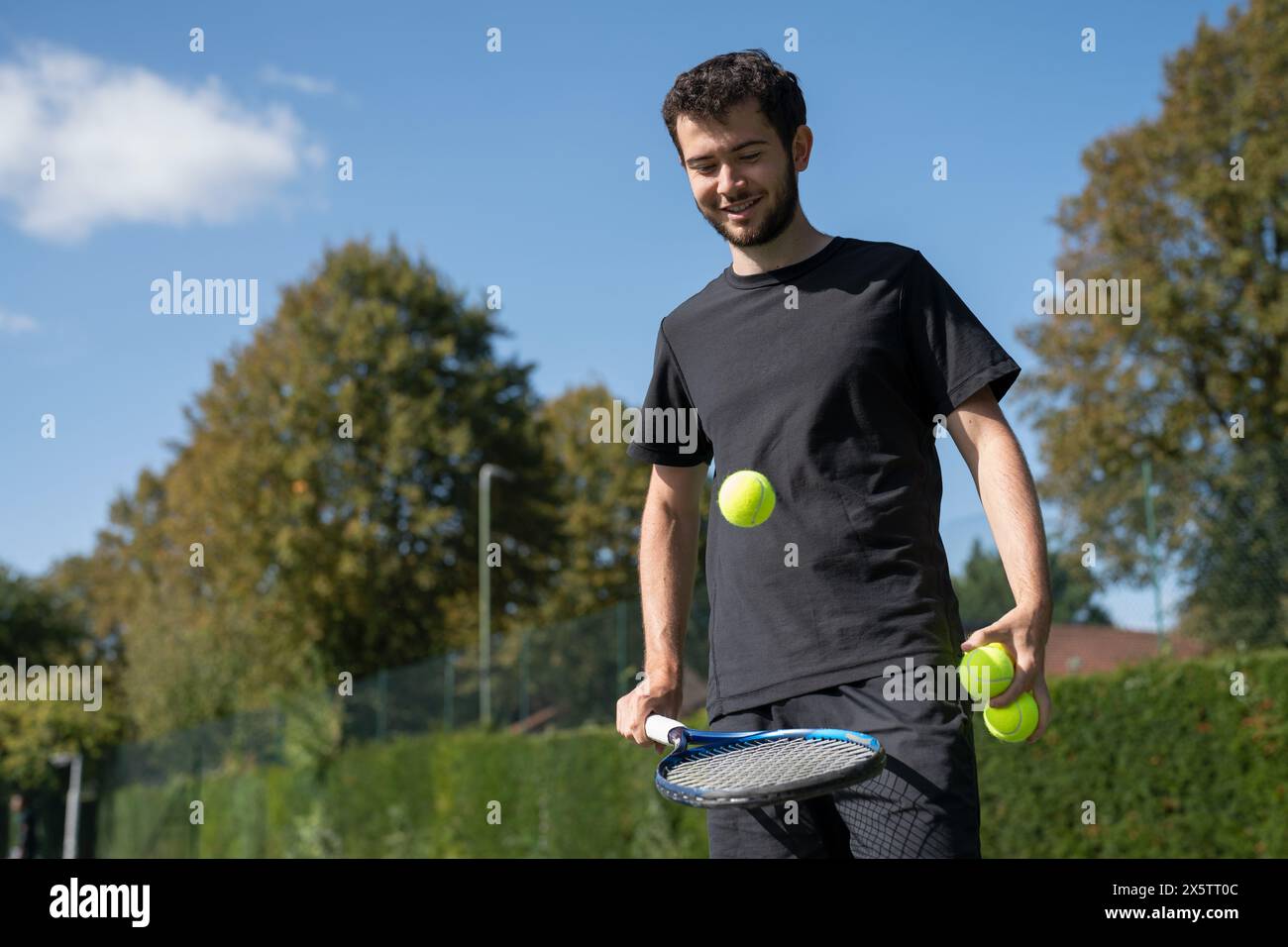 Smiling man bouncing tennis ball in tennis court Stock Photo - Alamy