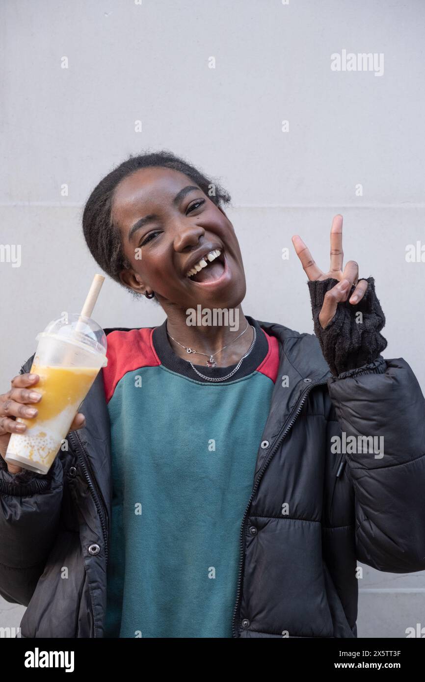 Portrait of cheerful young woman giving peace sign Stock Photo - Alamy