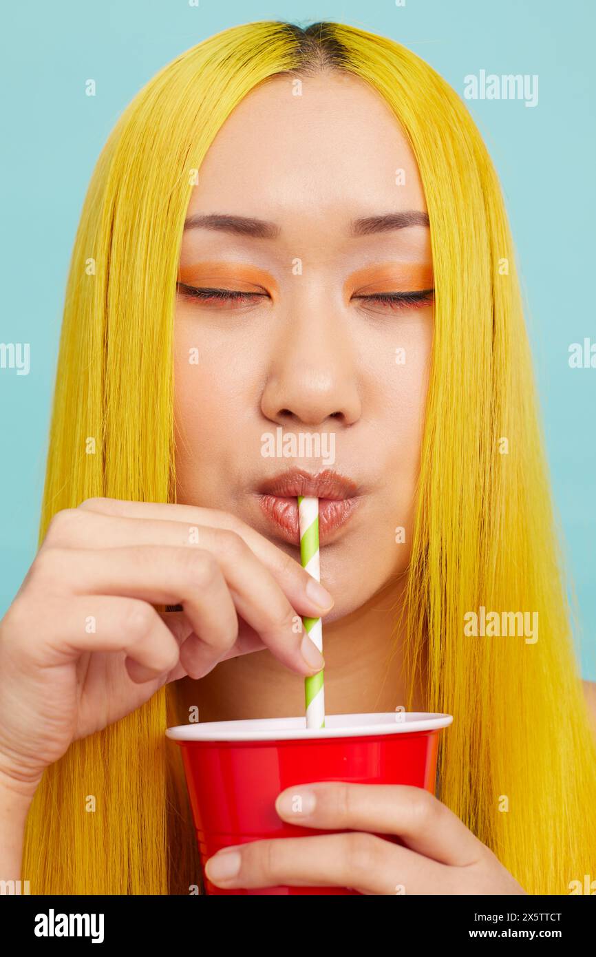 Young woman with long yellow hair and closed eyes, drinking through ...
