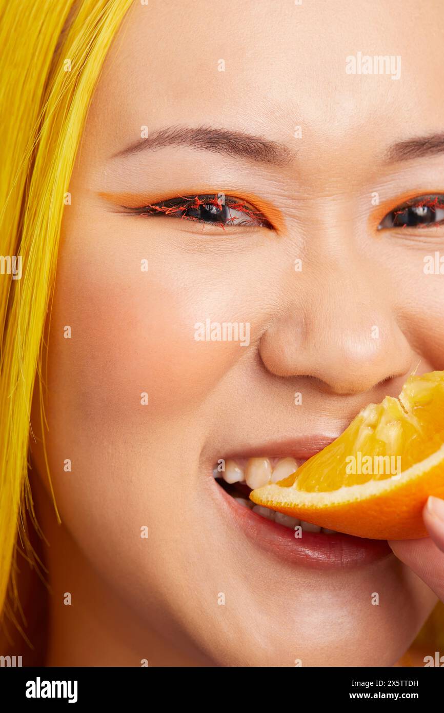 Young woman with orange make up, eating orange fruit Stock Photo - Alamy