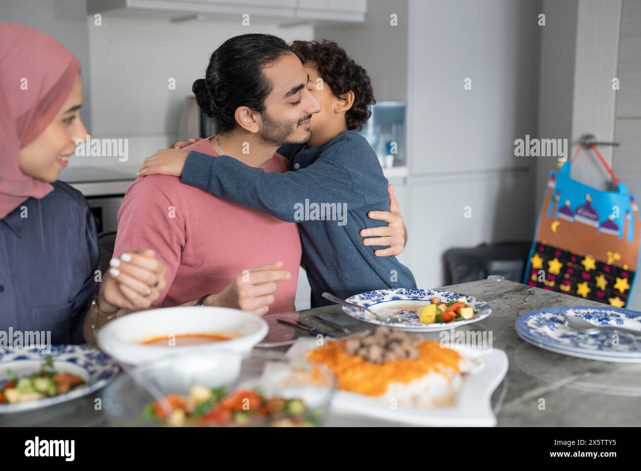 Boy (6-7) hugging father during family dinner Stock Photo - Alamy