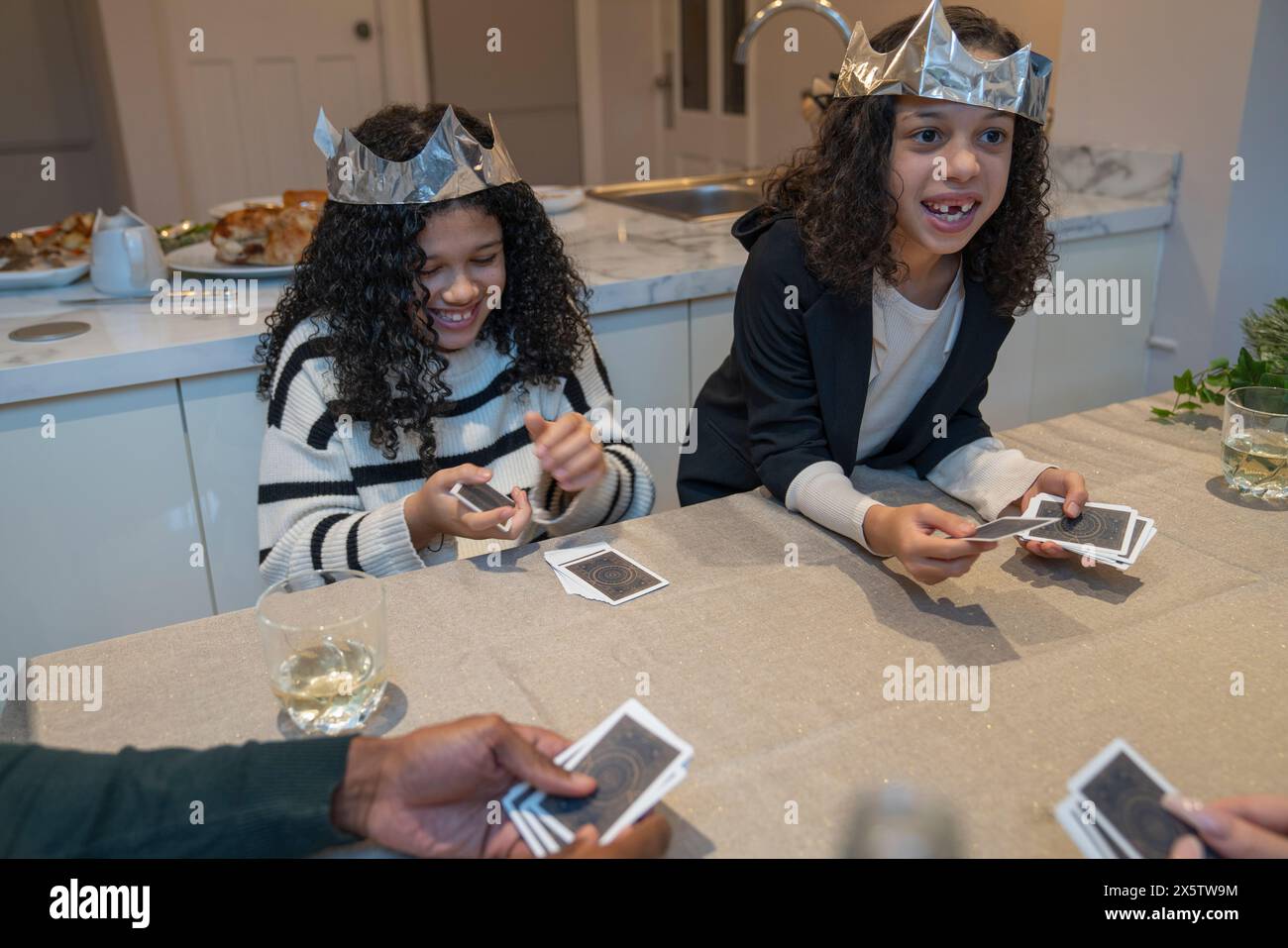 Smiling girls wearing paper crowns playing cards at table Stock Photo ...