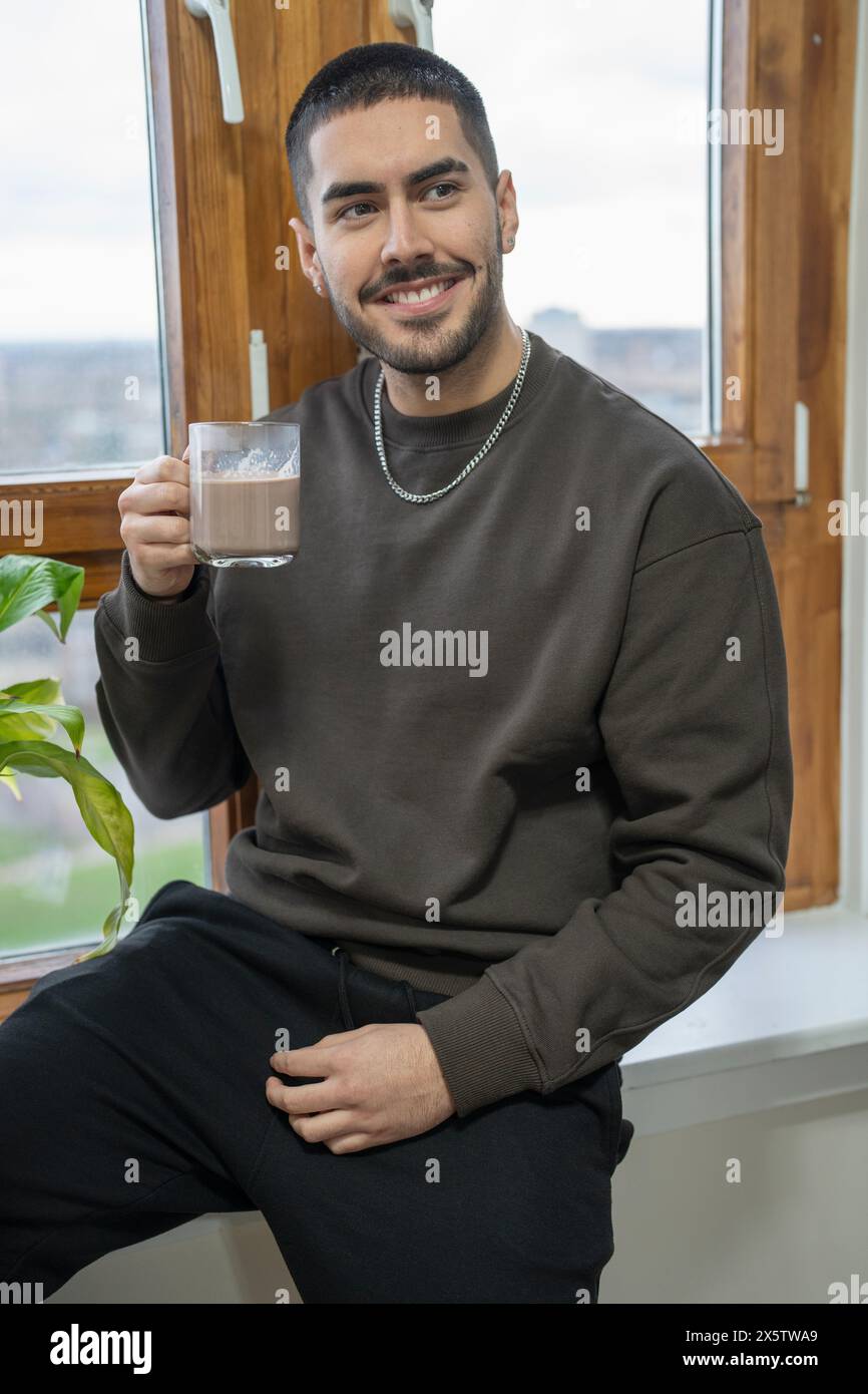 Smiling young man drinking milk tea at home Stock Photo - Alamy
