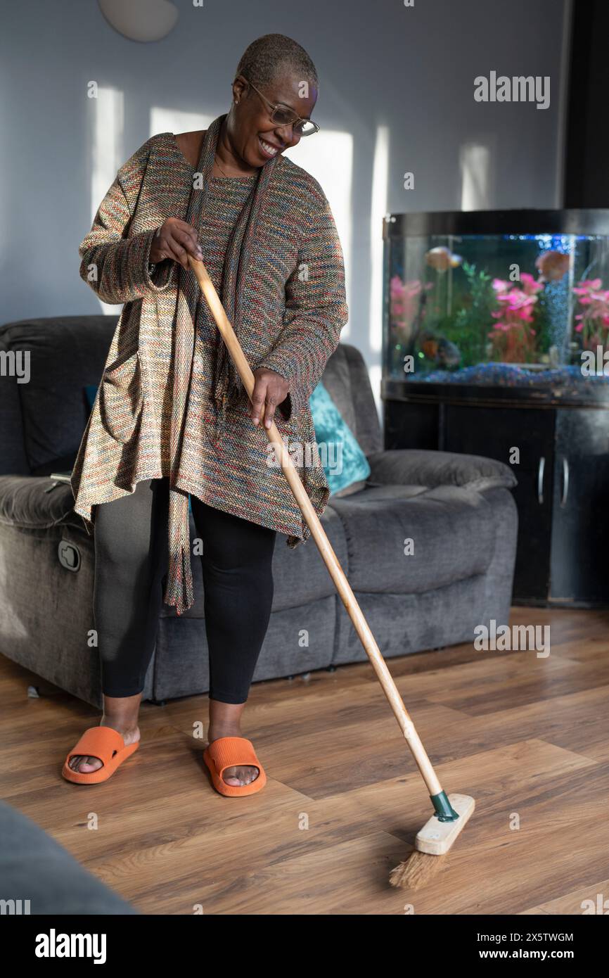 Mature woman sweeping floor in living room Stock Photo - Alamy