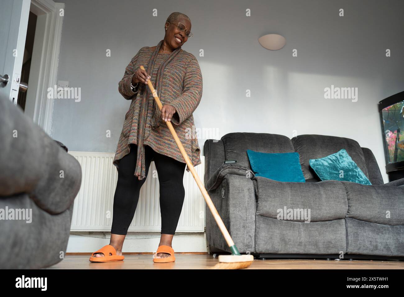Mature woman sweeping floor in living room Stock Photo - Alamy