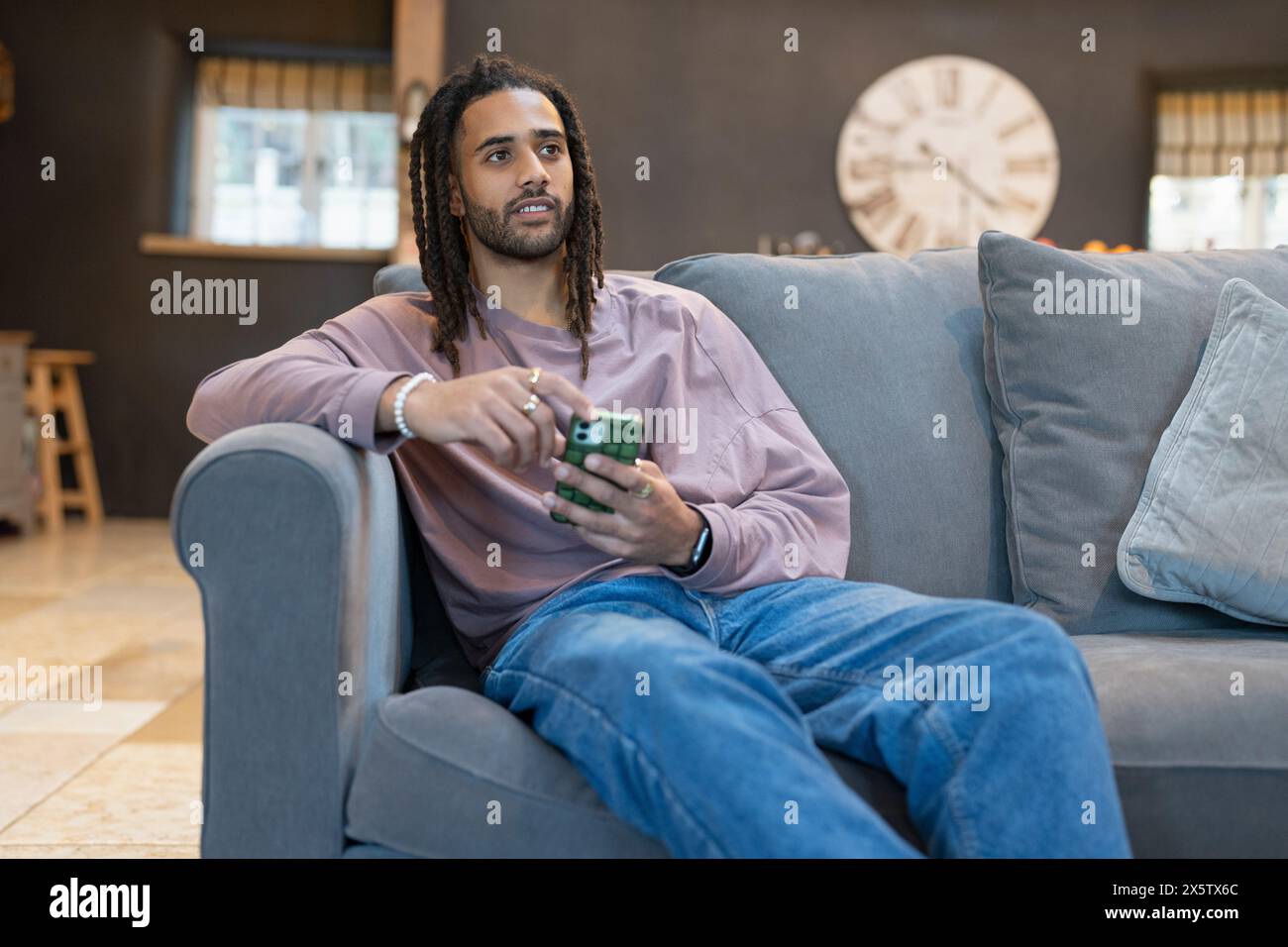 Man with dreads relaxing on sofa and using phone Stock Photo - Alamy